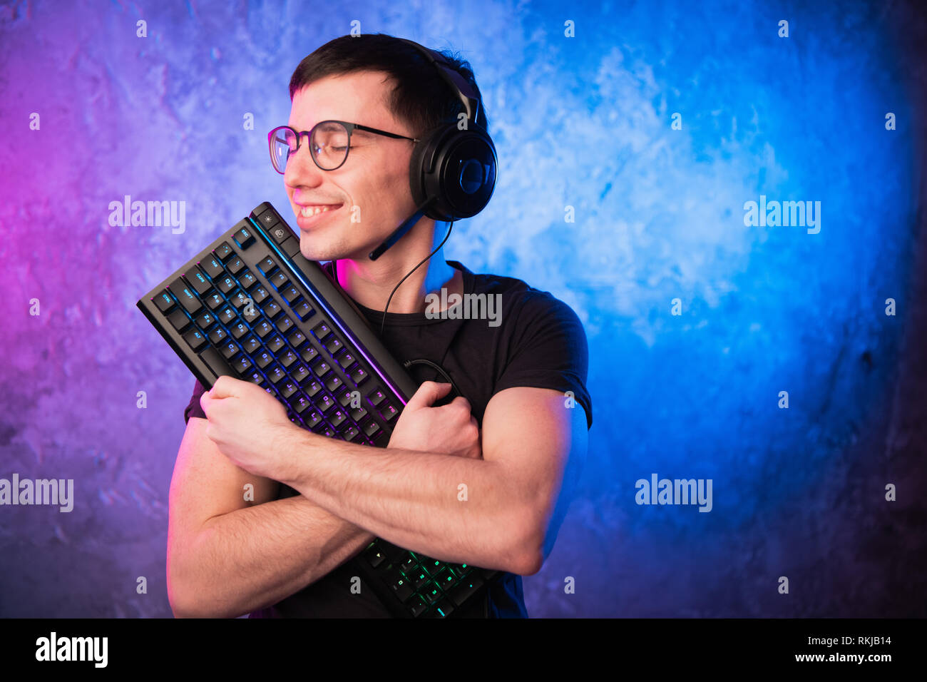 Computer nerd with keyboard over colorful pink and blue neon lit wall ...