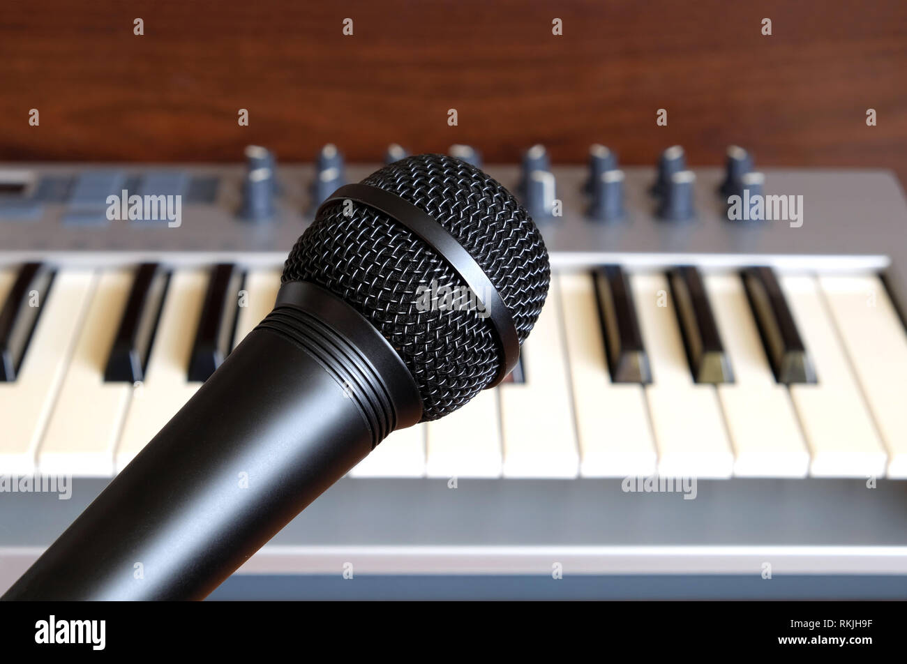 Black vocal microphone close up against electronic synthesizer keyboard ...
