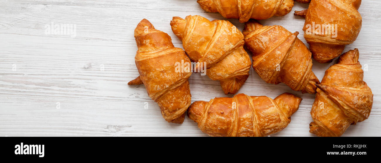 Freshly baked golden croissants on white wooden surface, top view. Flat ...