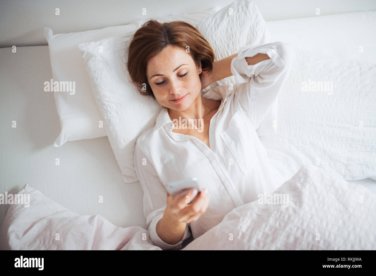 A top view of young woman lying in bed indoors in a bedroom, using ...