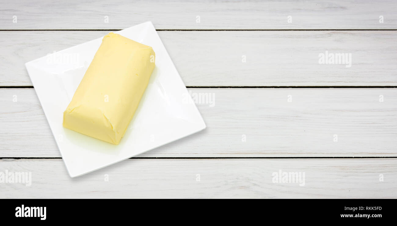 Top view of a plate with natural butter portion on a wooden white table ...