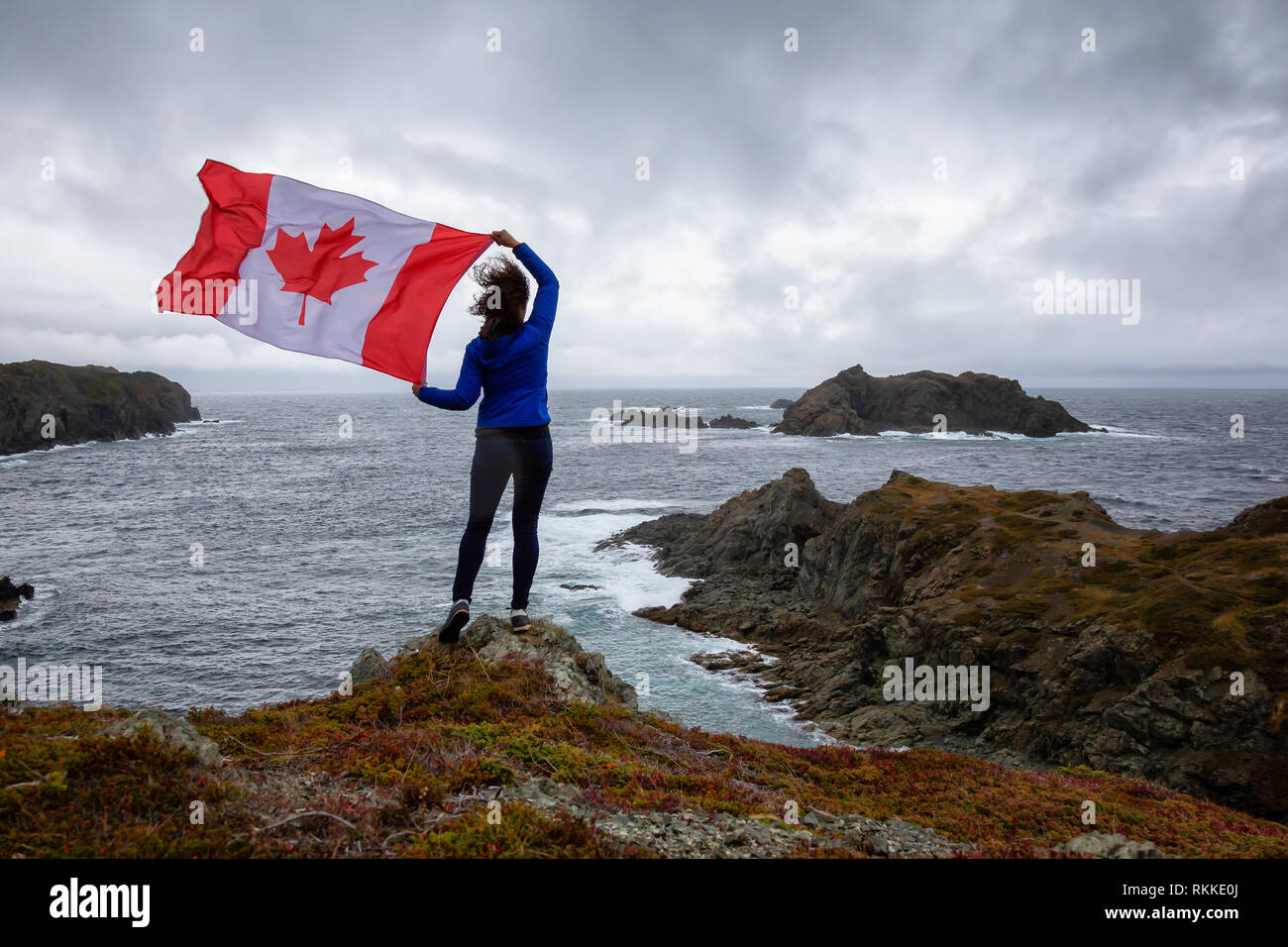 Adventurous woman holding a Canadian Flag on a Rocky Atlantic Ocean ...