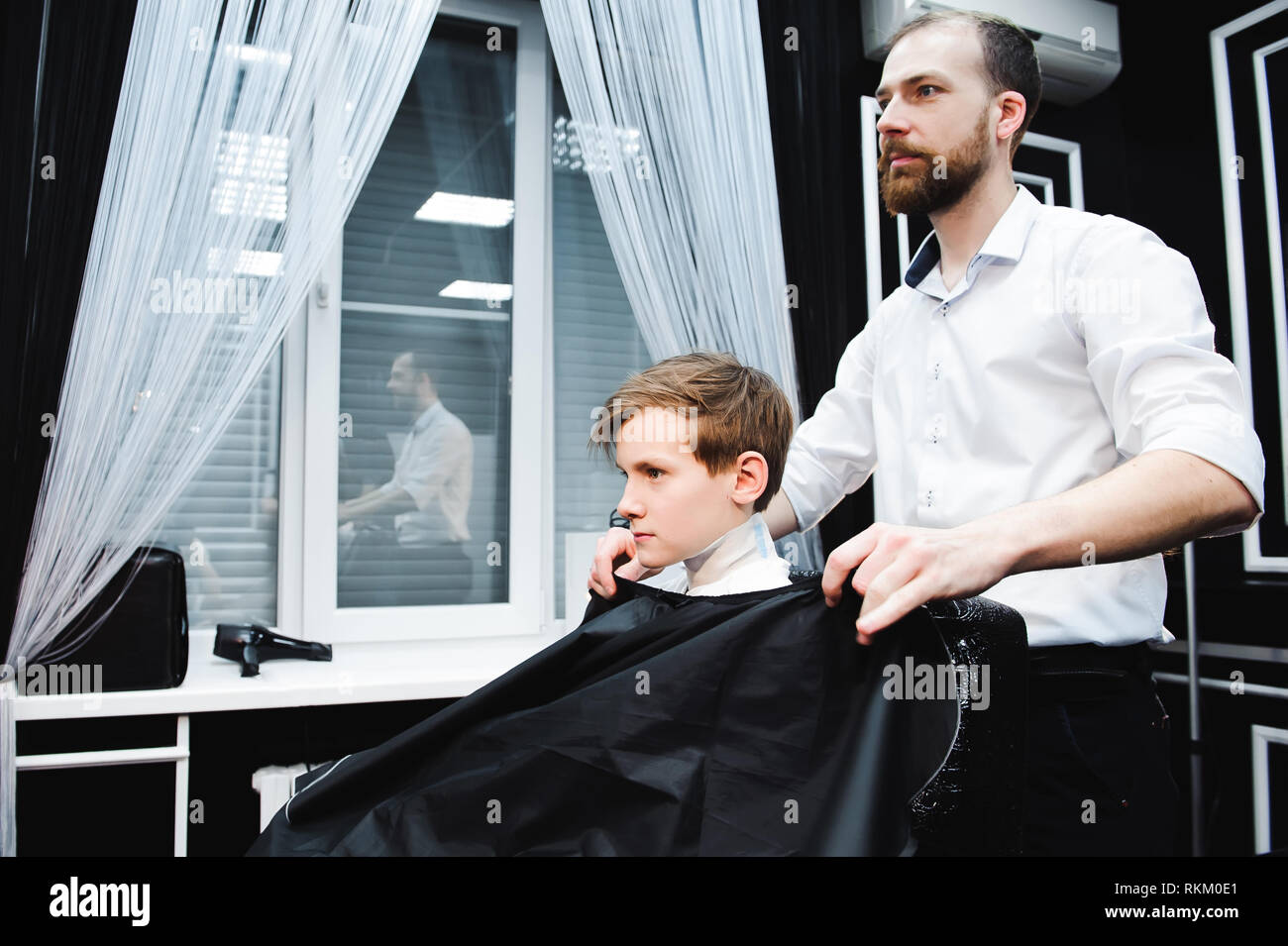 Young handsome barber making haircut of cute boy in barbershop Stock ...