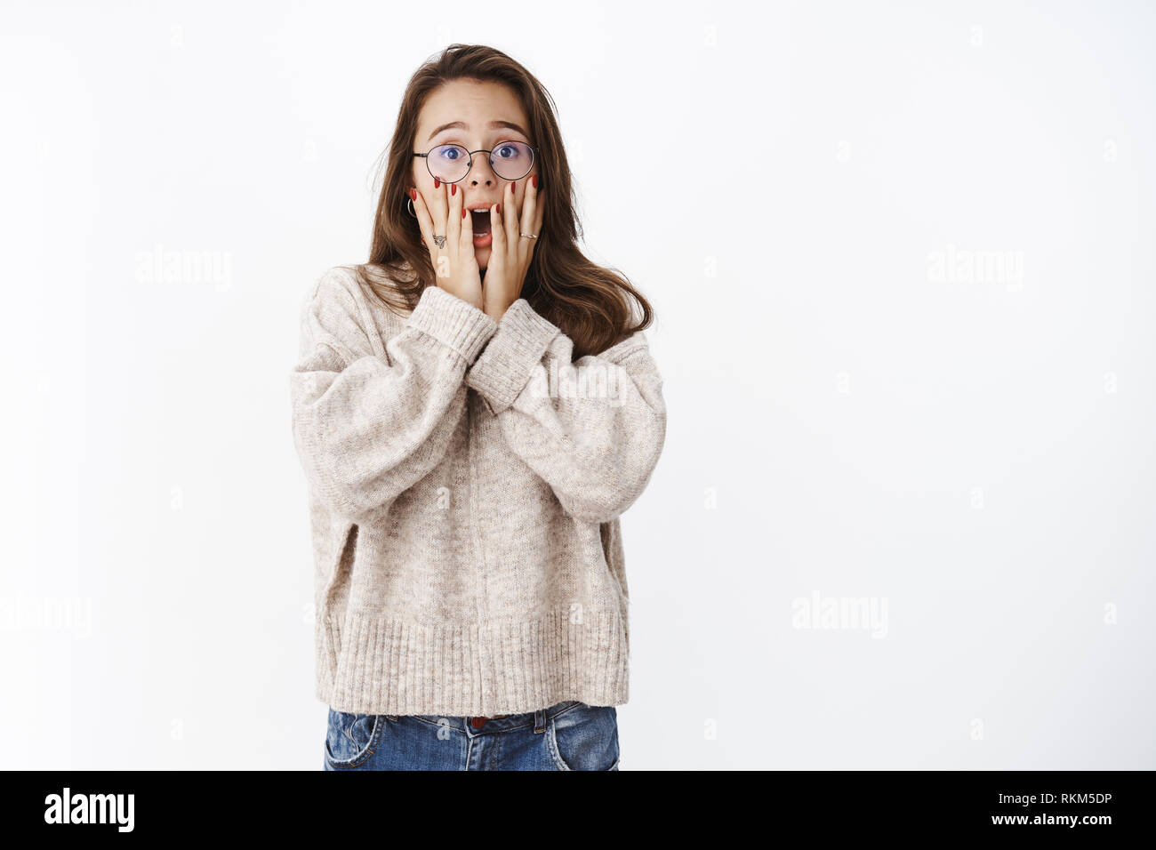 Indoor shot of freaked out shocked and amazed young woman in glasses ...