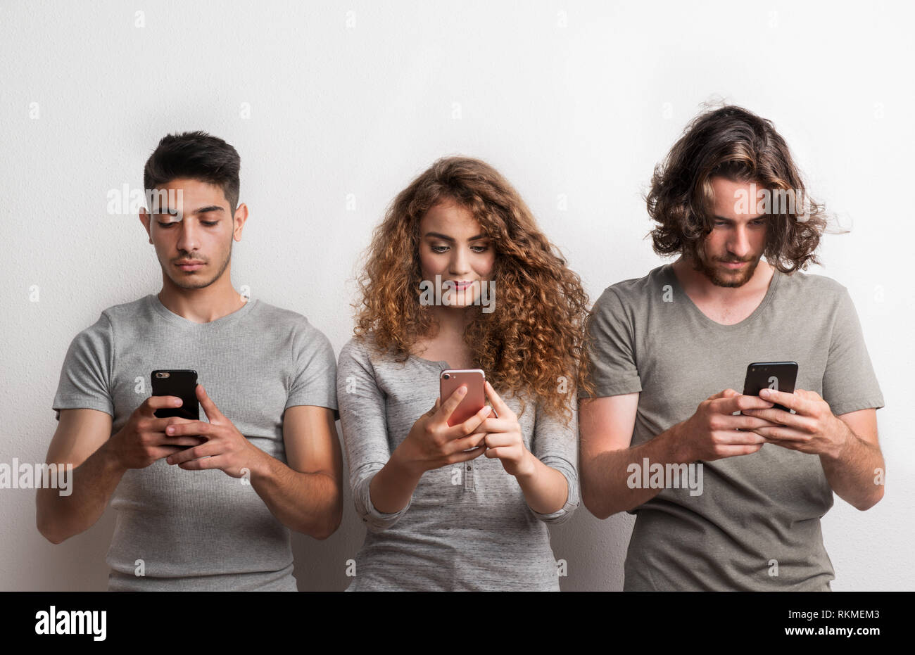 Portrait of young girl with two boy friends standing in a studio, using ...