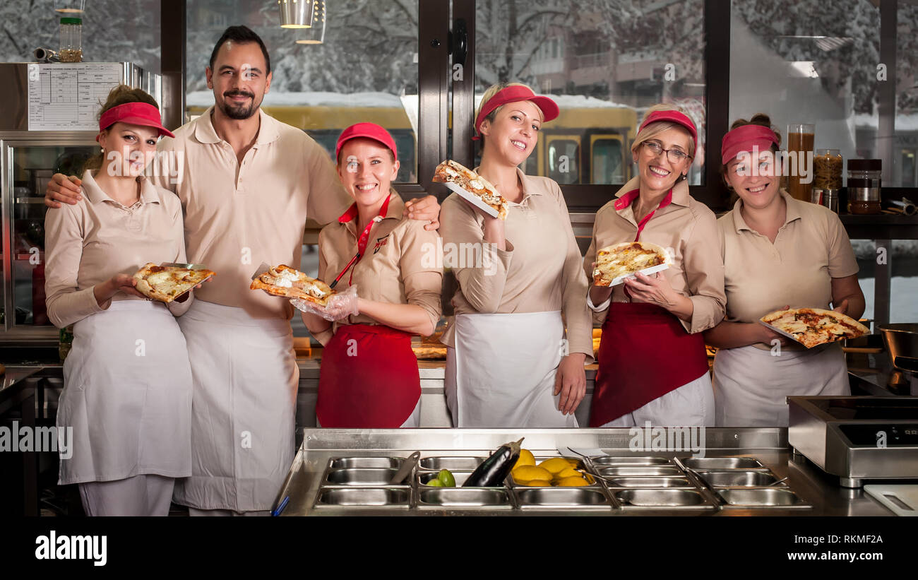 Smiling young stuff aprons selling pizza in fast food restaurant. Tasty ...
