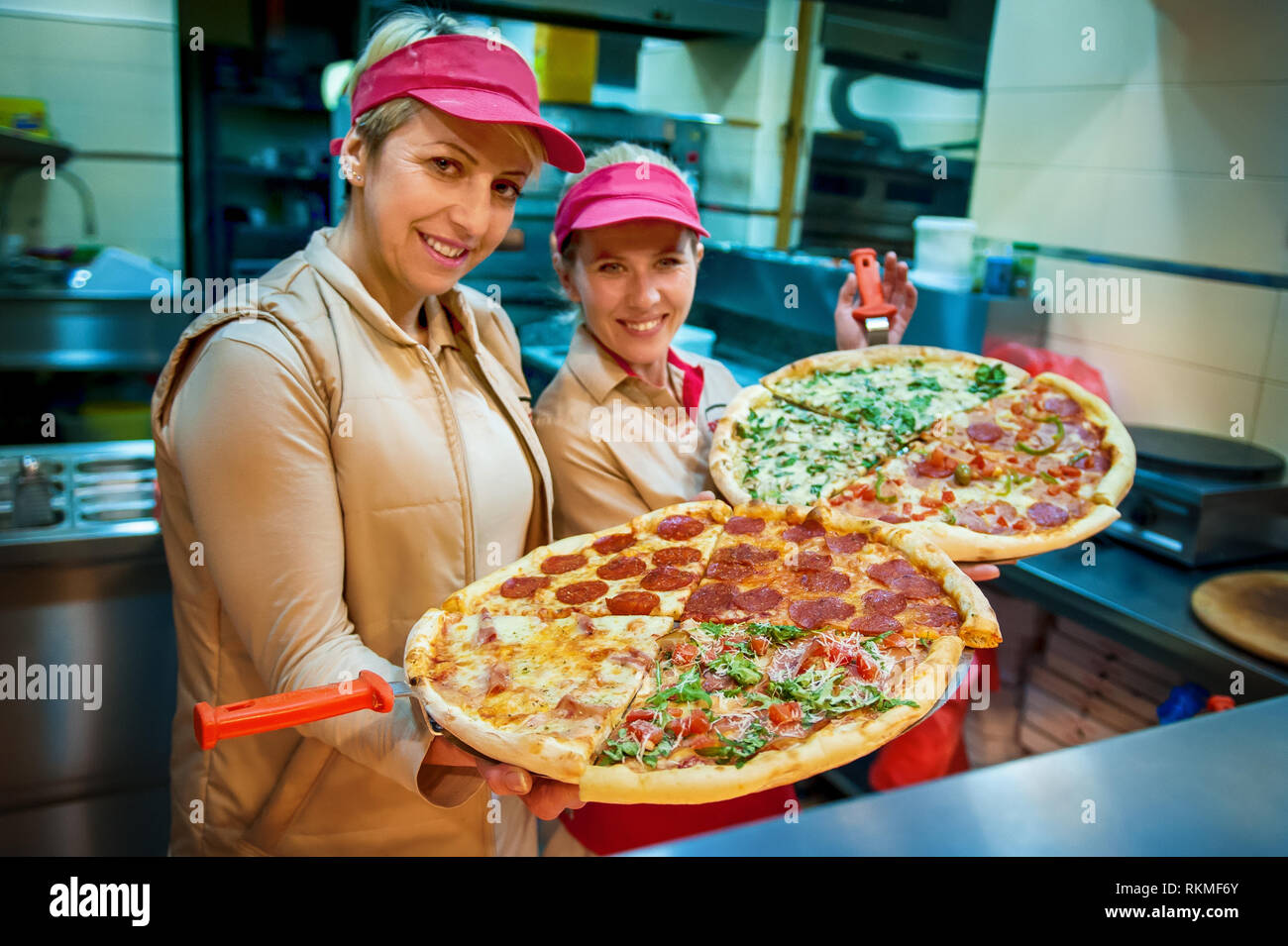 Two smiling woman workers selling pizza in fast food restaurant. Tasty ...