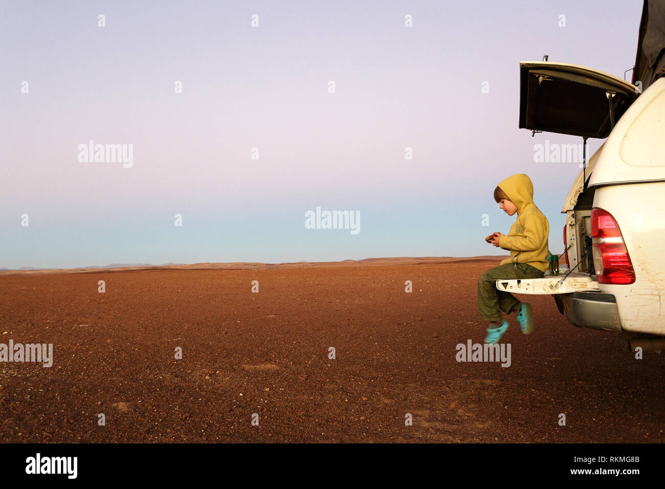 Little boy having a snack on the trunk of a 4x4 wheel drive car in dry ...