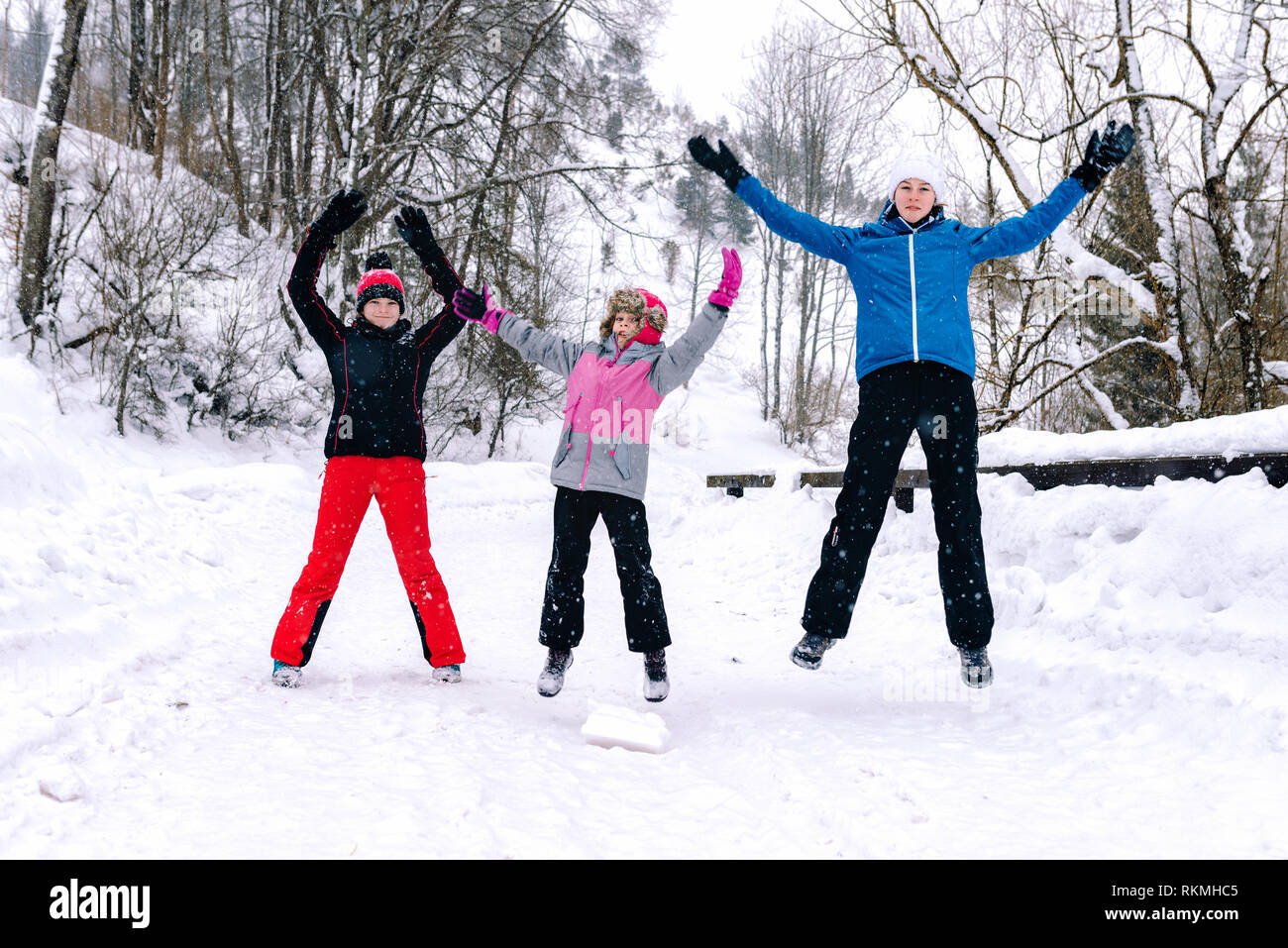 Three friends joyfully jump over snowdrifts in the winter in the ...