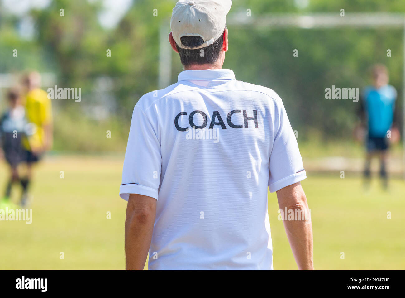 Back of male football coach wearing white COACH shirt at an outdoor ...