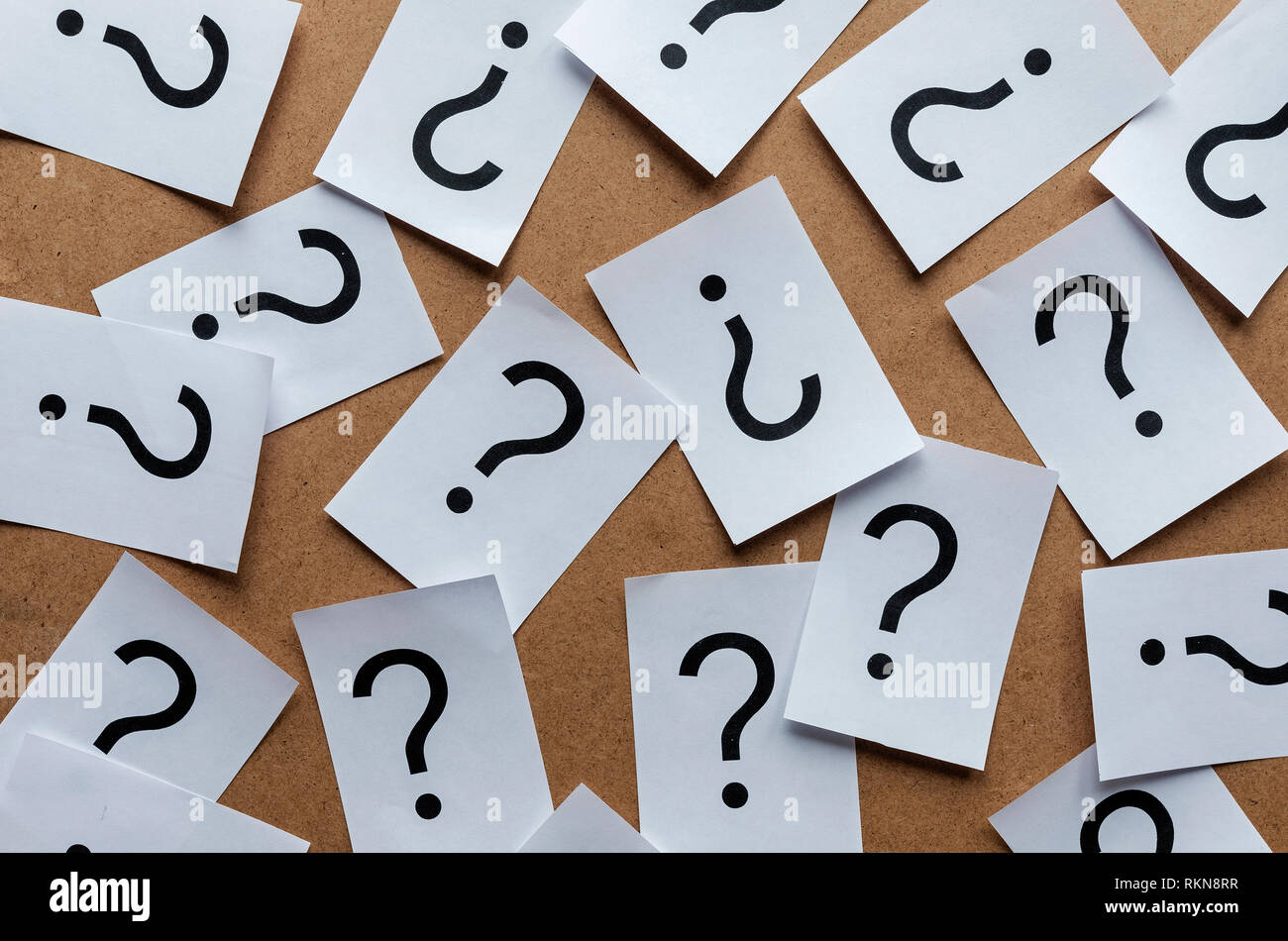 black question marks on paper cards scattered randomly over a wooden ...