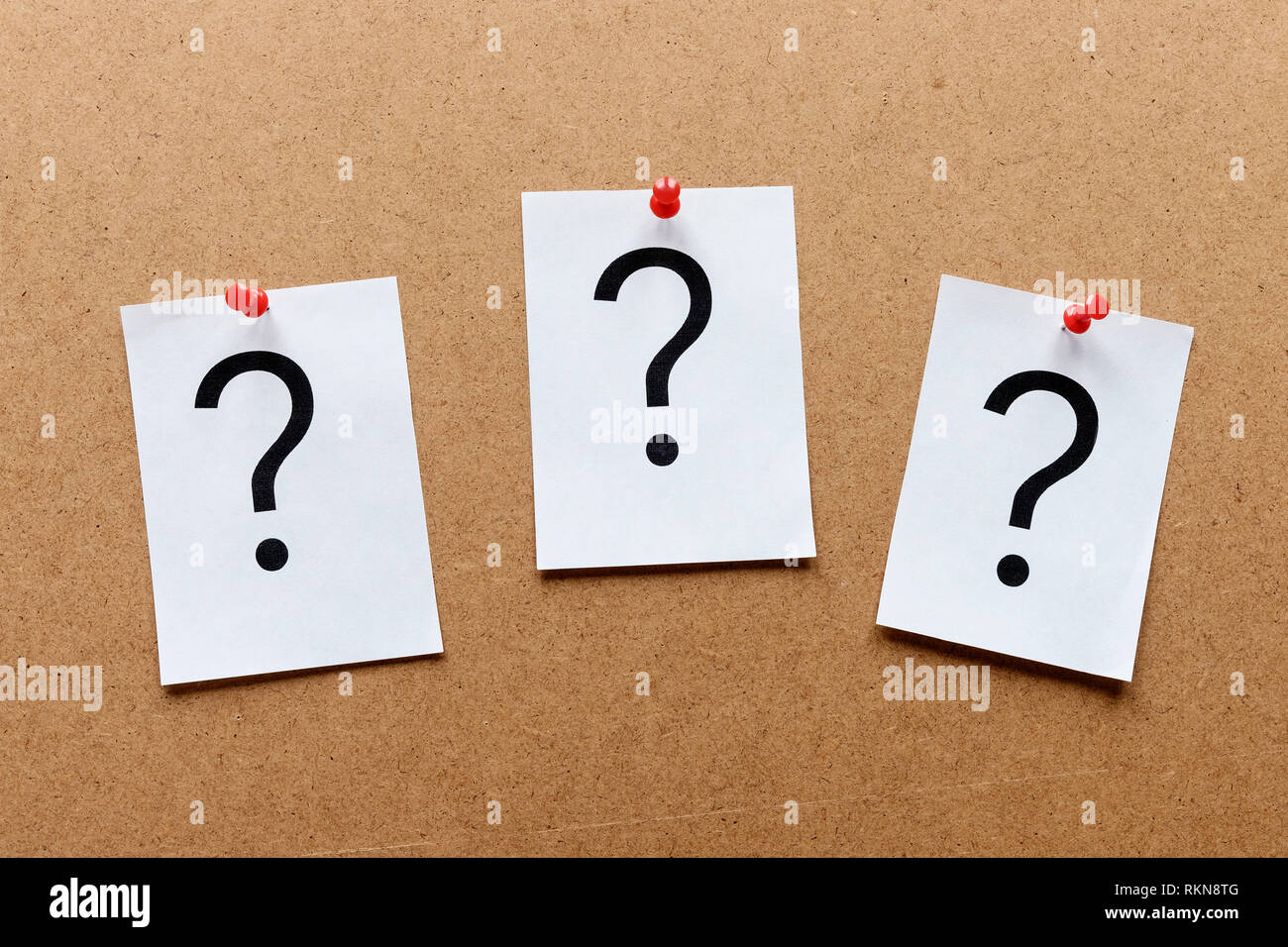 Three question marks pinned in a row with colorful red thumb tacks on a ...