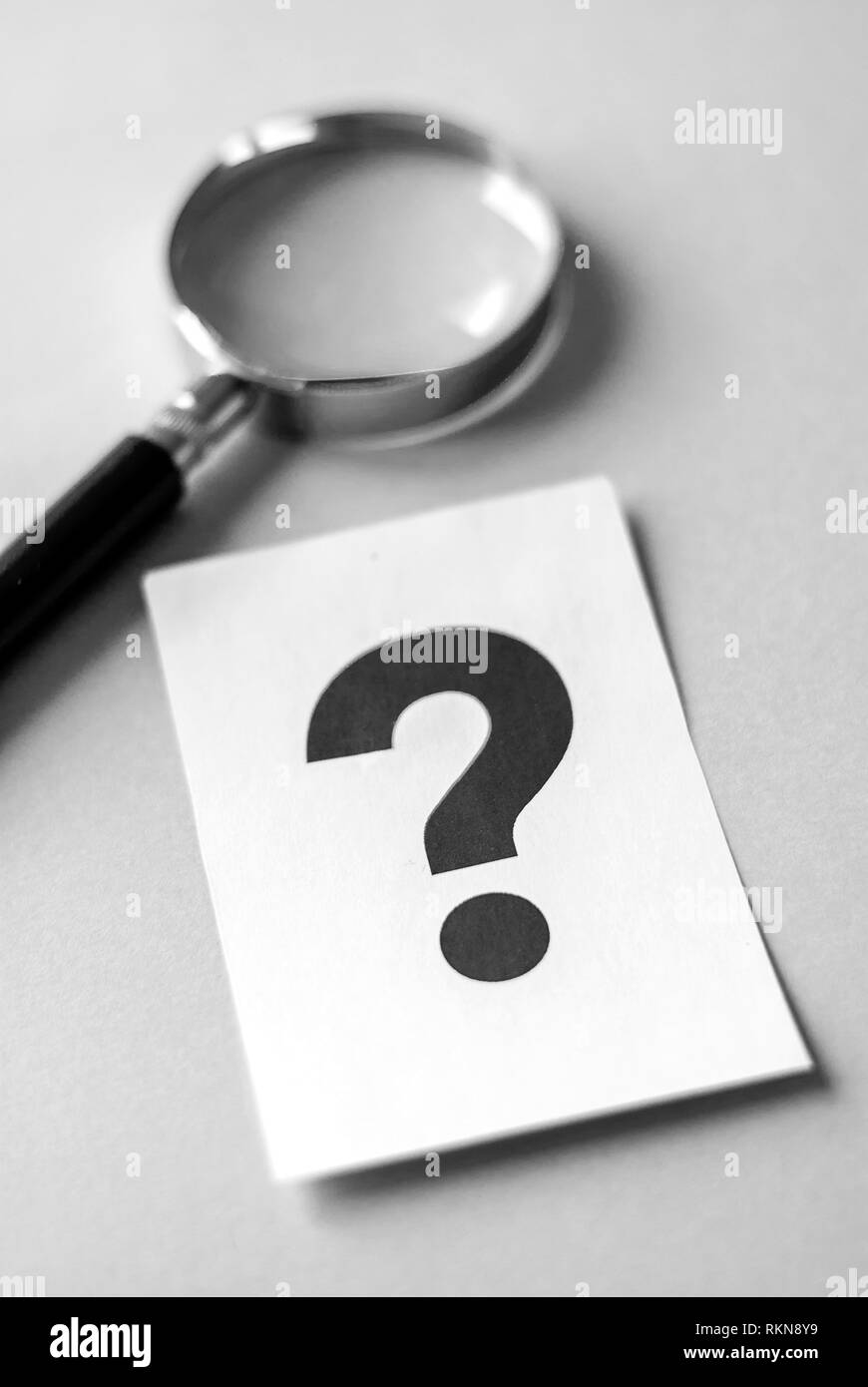 Magnifying glass on grey surface, next to big black question mark ...