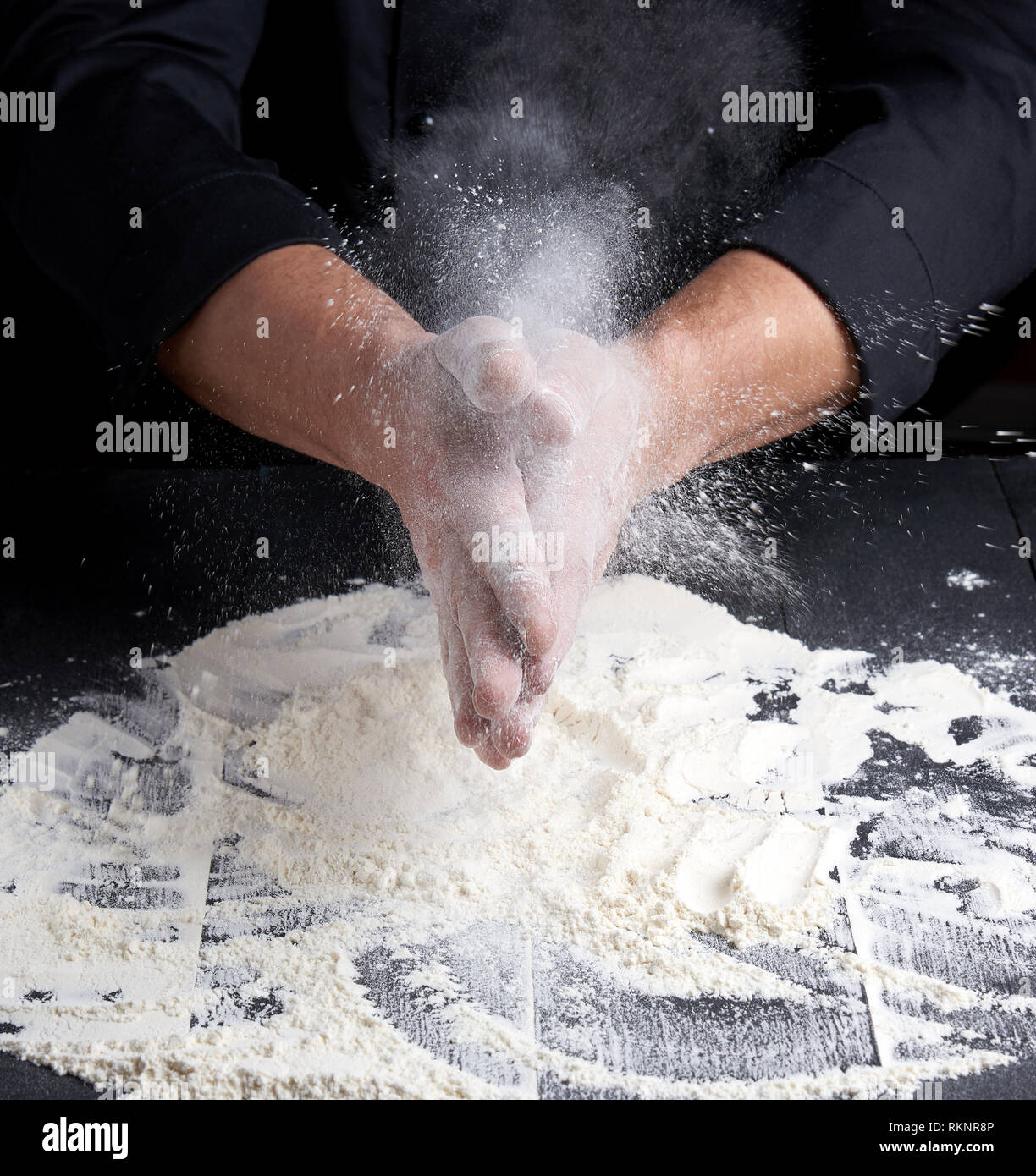 chef in black uniform pours white wheat flour out of his hands on a ...