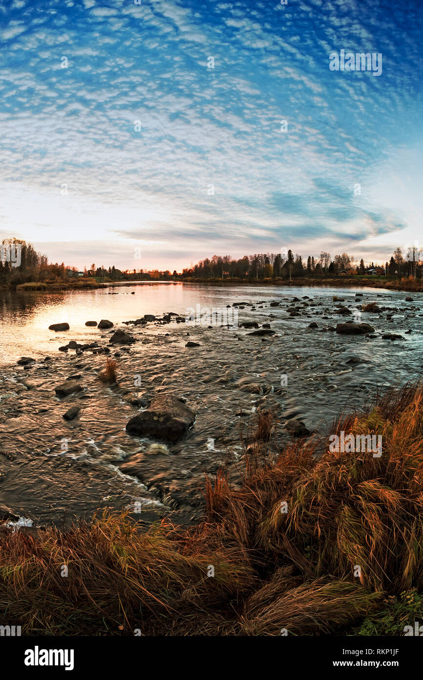 The autumn sun sets behind the river and the light reflects on the ...