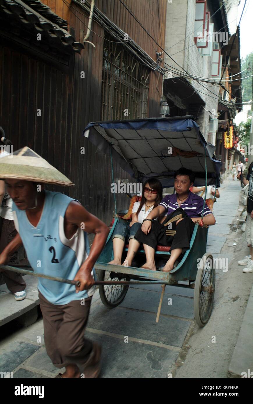 A rickshaw driver pulling tourists through the backstreets of Fenghaung ...