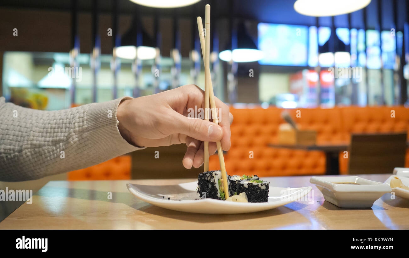 Young guy with chopsticks takes sushi from a plate in a japanese ...