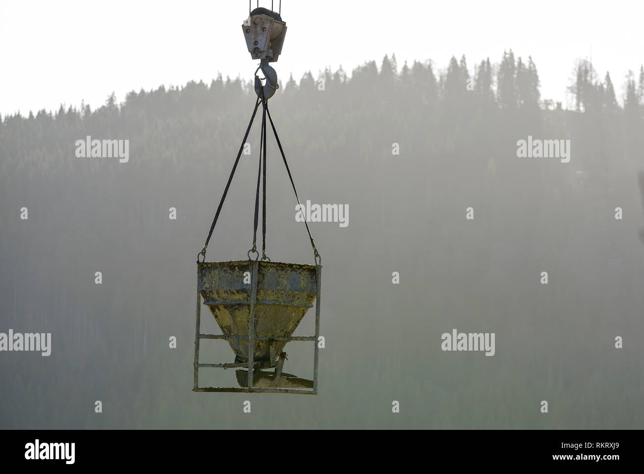 Bucket container with liquid concrete hanging on crane hook on copy ...
