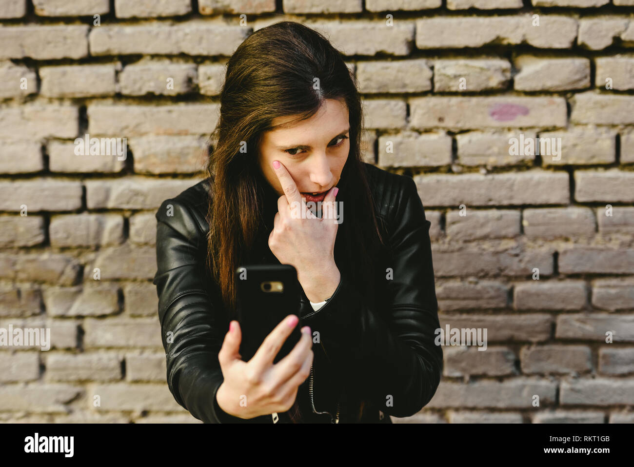 Young girl using the screen of her mobile phone as a mirror to put on ...