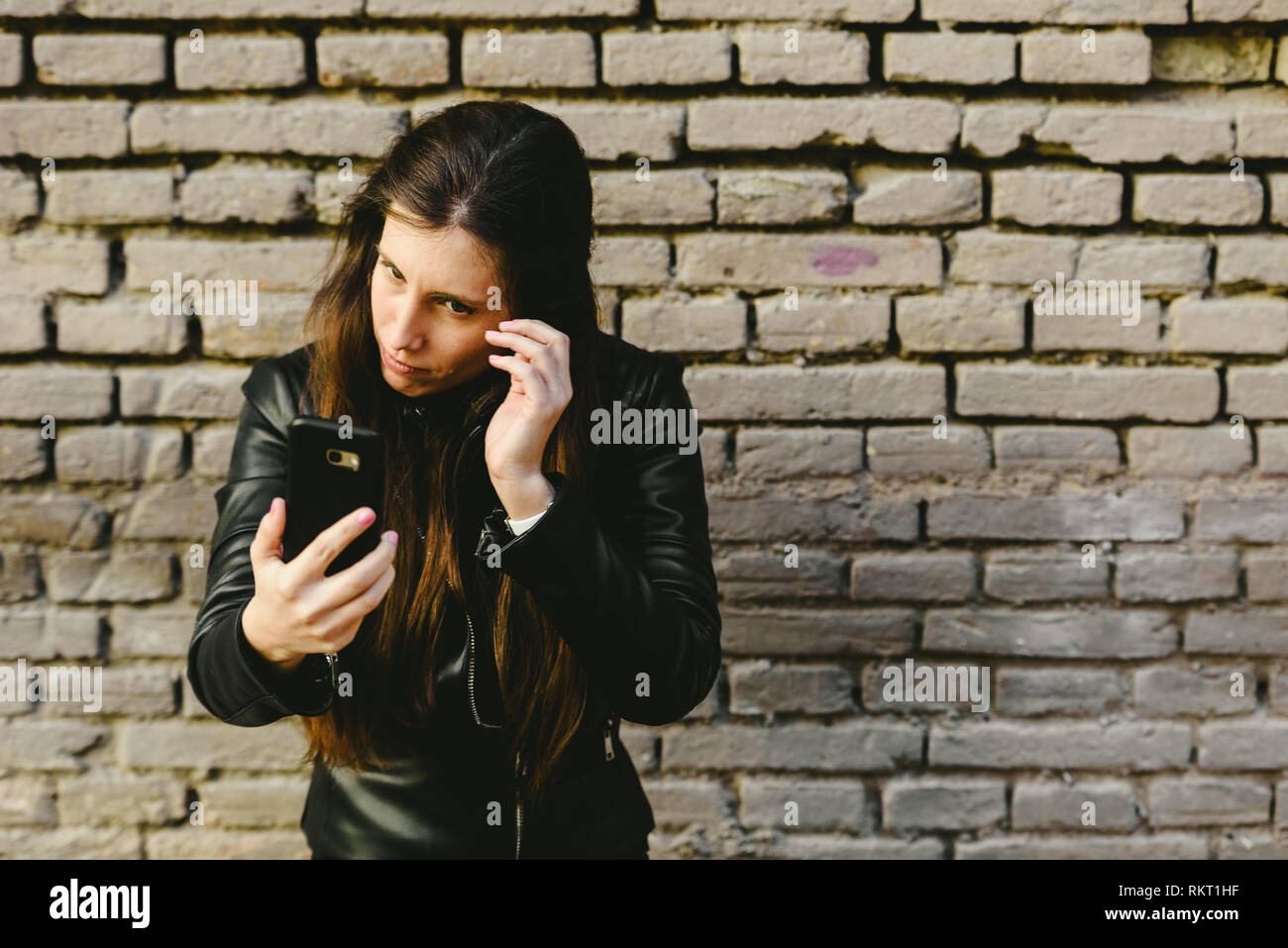 Young girl using the screen of her mobile phone as a mirror to put on ...
