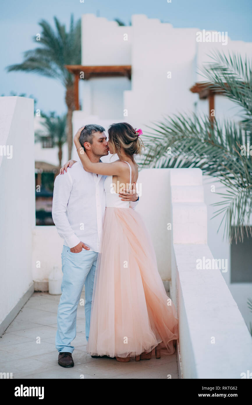 Happy newlyweds kiss on terrace of white villa against background of ...