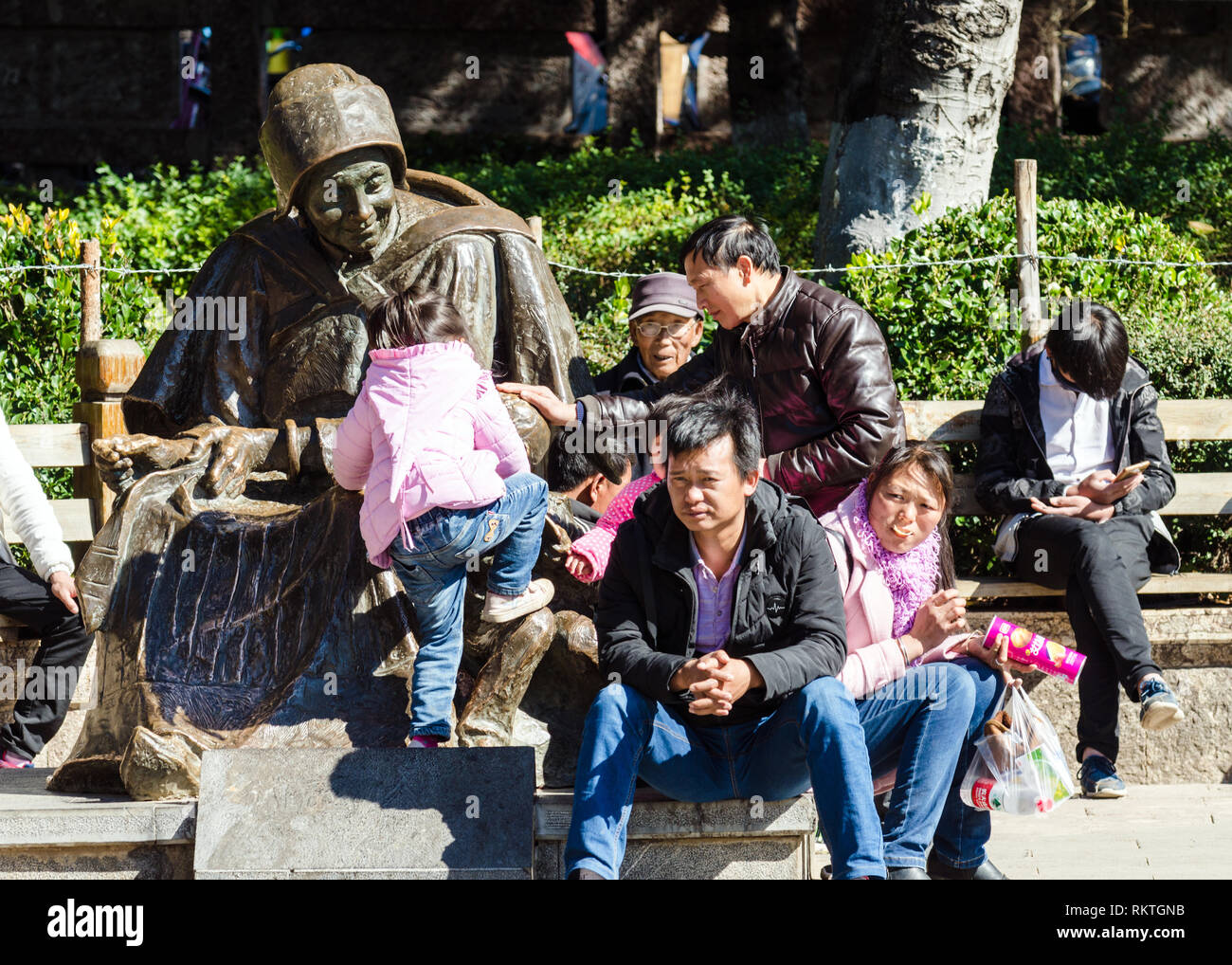 Locals sitting around a statue in Yuhe square, Lijiang, Yunnan, China ...