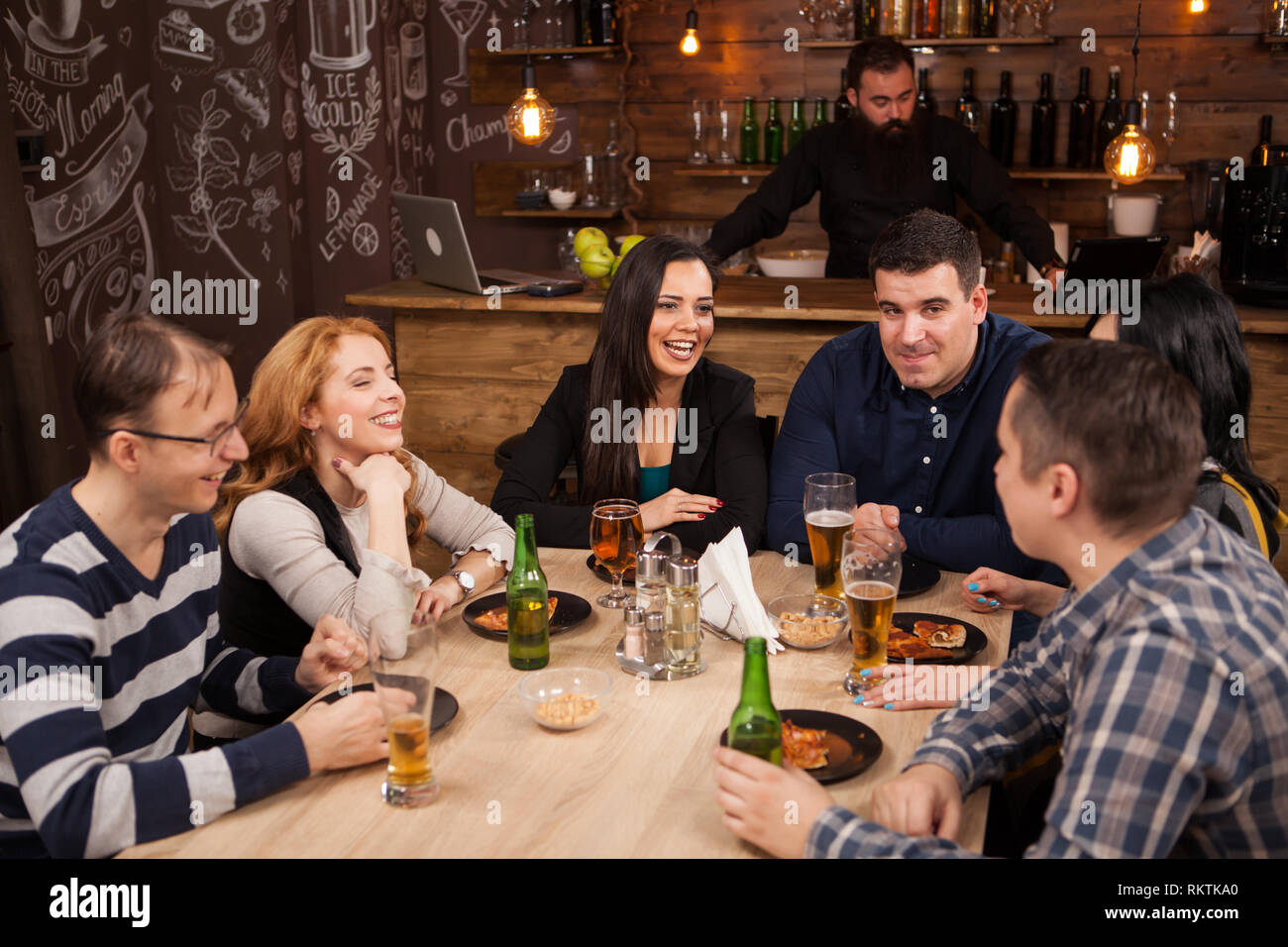 Group of young friends sitting around table in bar togethe. Cheerful ...
