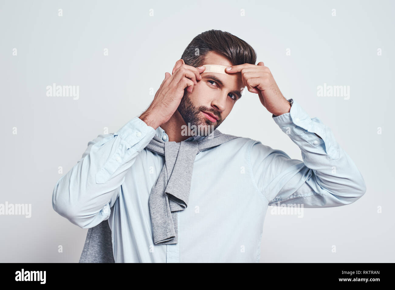 Oops...Bearded young man in casual wear is putting band-aid on his ...