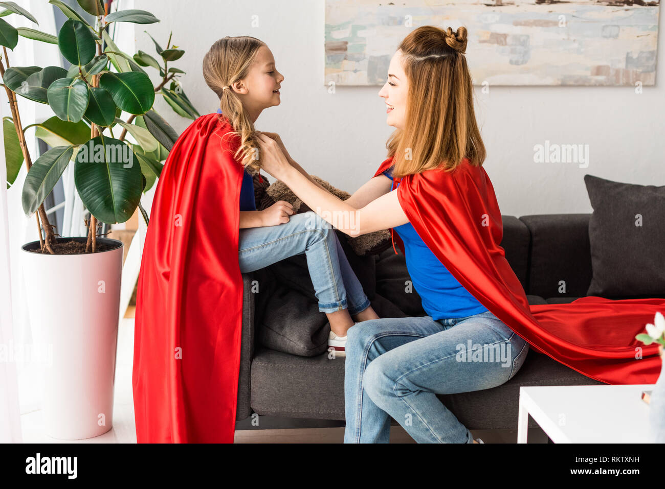 Beautiful mother tying red cloak on daughter at home Stock Photo - Alamy