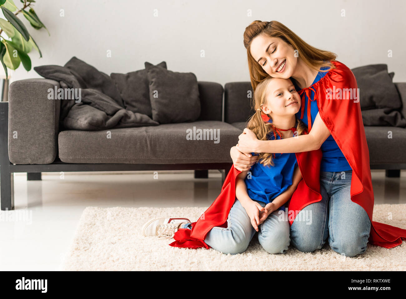 Kid and mother in red cloaks sitting on floor and hugging at home Stock ...