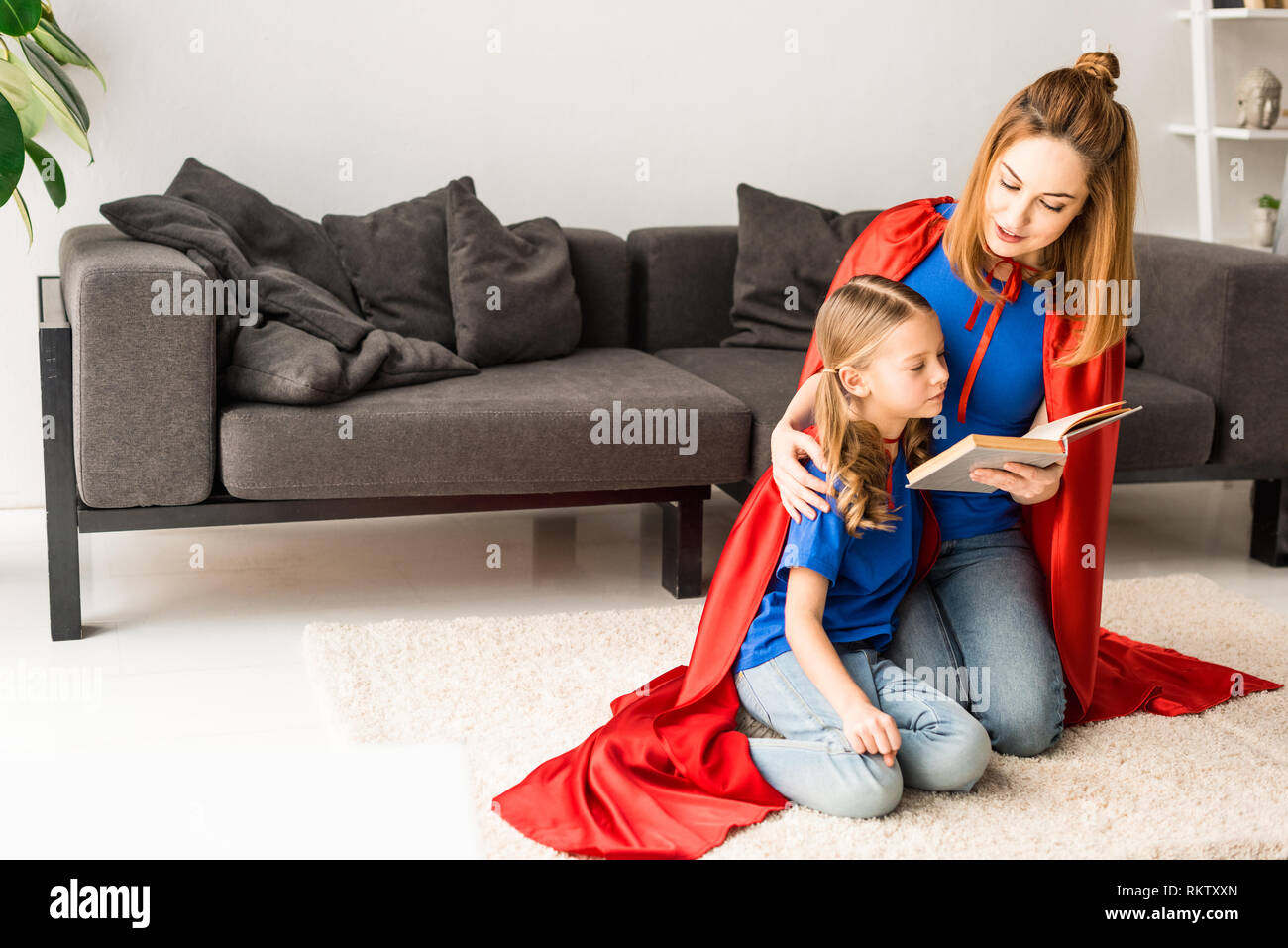 kid and mother in red cloaks sitting on floor and reading book Stock ...