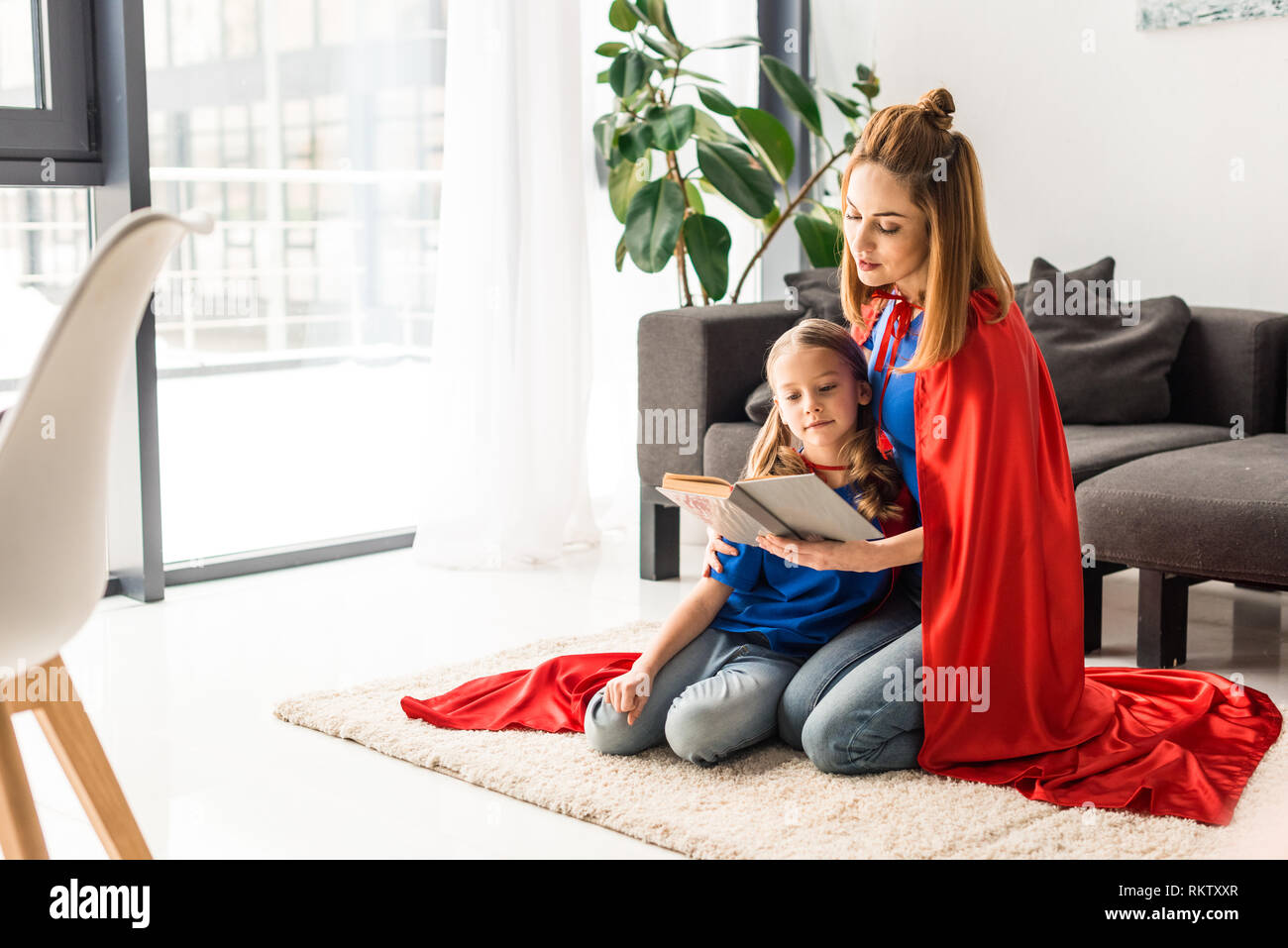 daughter and mother in red cloaks sitting on floor and reading book ...