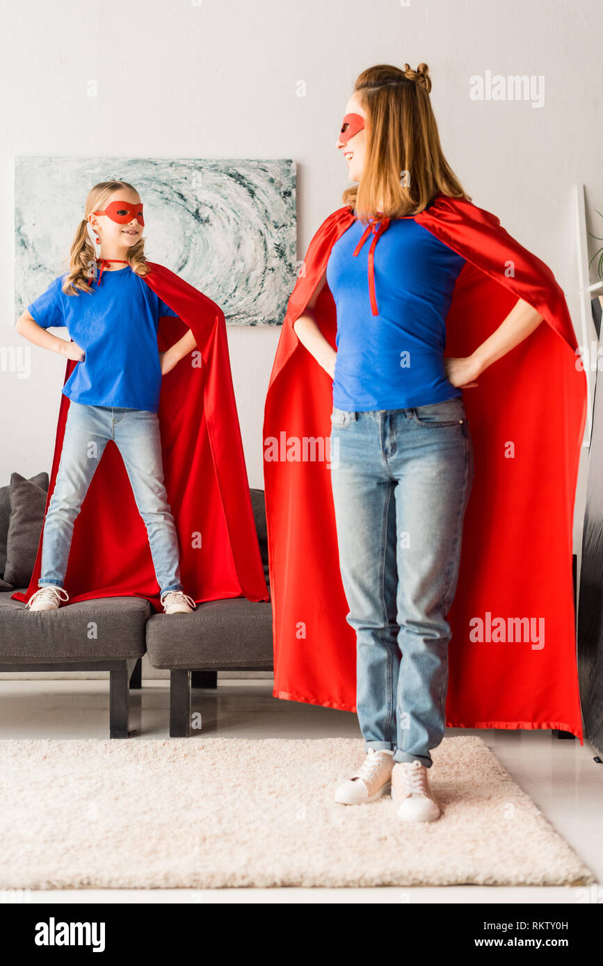 Cute daughter and mother in red cloaks and masks looking at each other ...