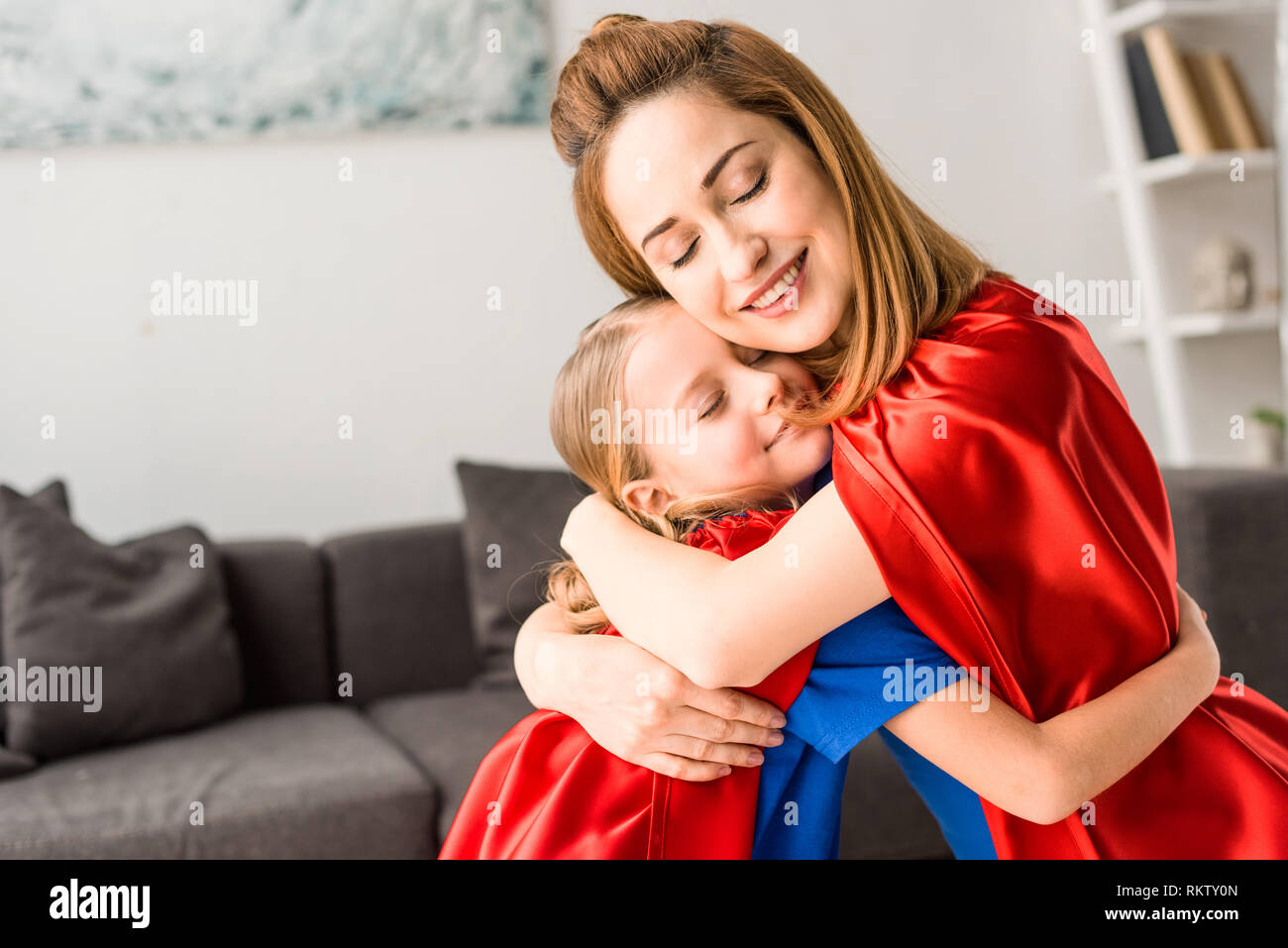 kid and mother in red cloaks hugging and smiling at home Stock Photo ...