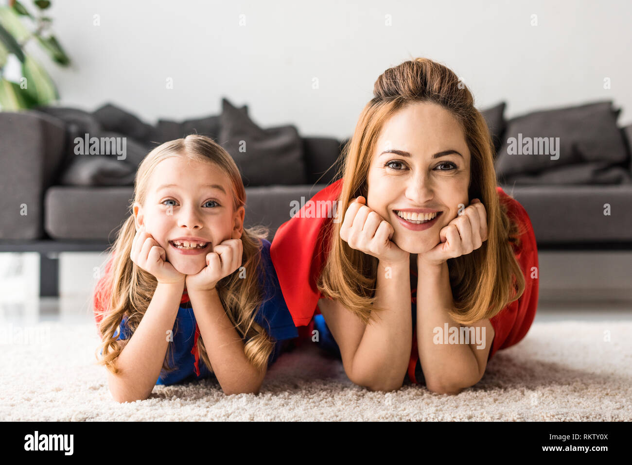 Smiling daughter and mother looking at camera on floor Stock Photo - Alamy