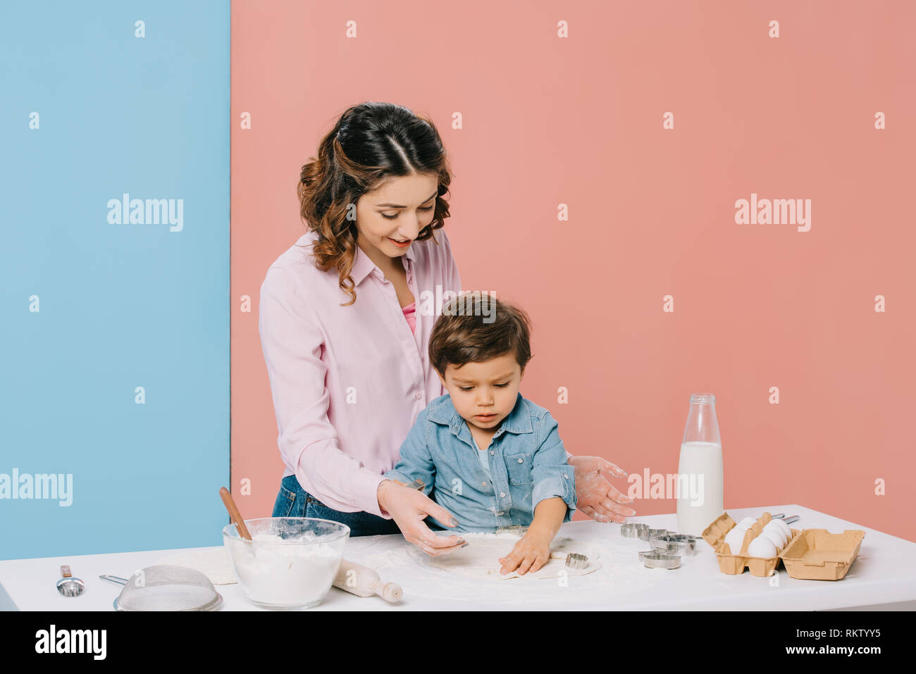 smiling mother with cute little son cooking pastry together on bicolor ...