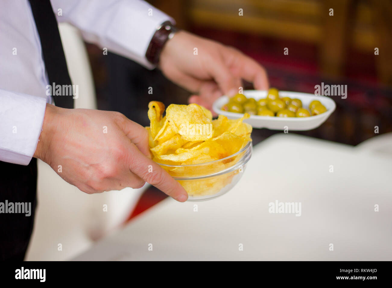 the hands of a waiter serving chips and olives Stock Photo - Alamy