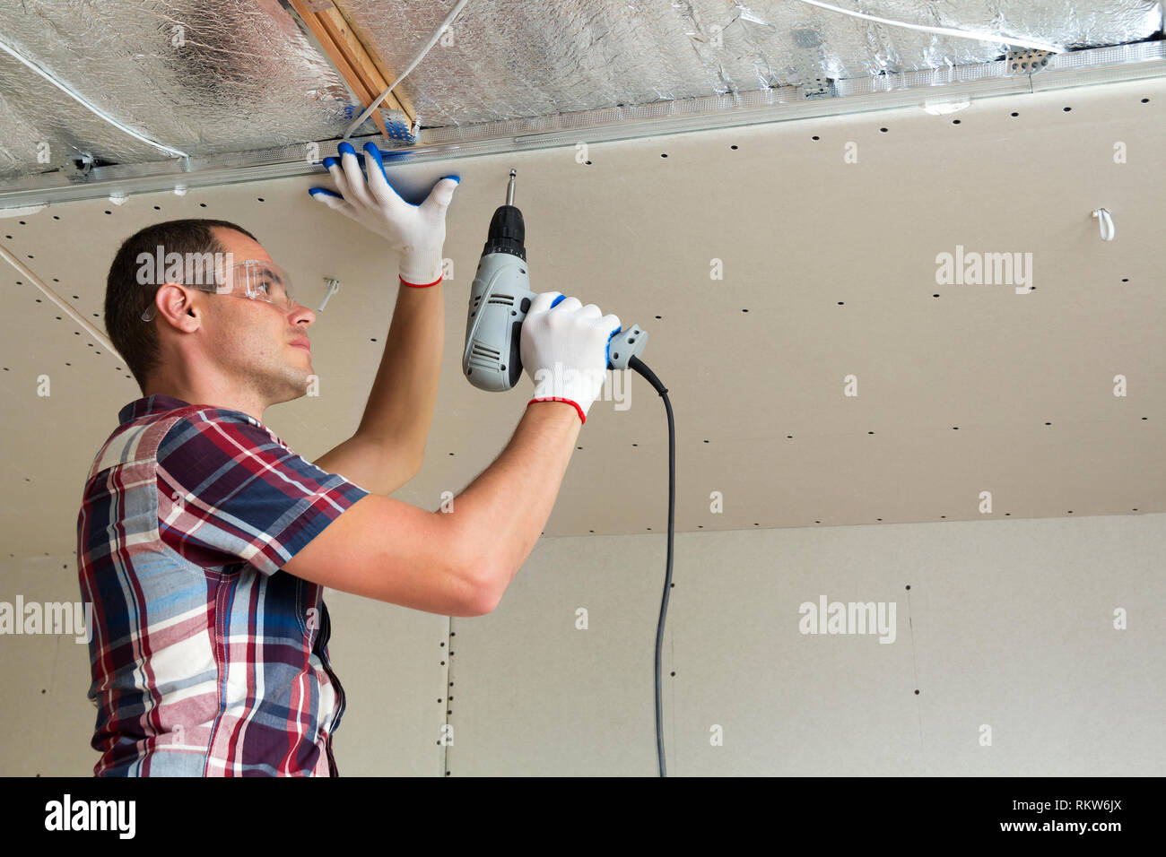 Young man in goggles fixing drywall suspended ceiling to metal frame ...
