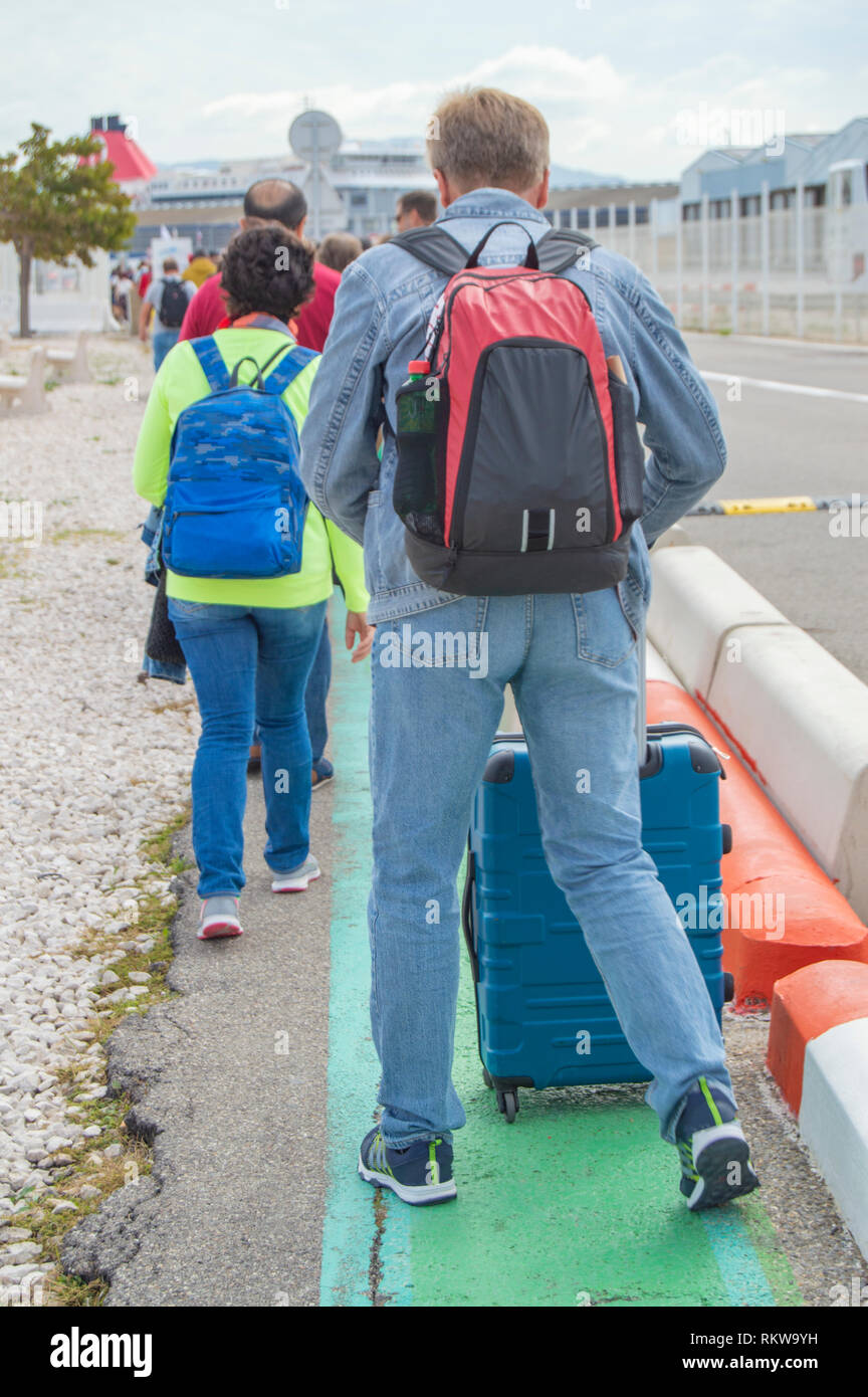 Happy tourists with backpacks and suitcases are moving along the road ...
