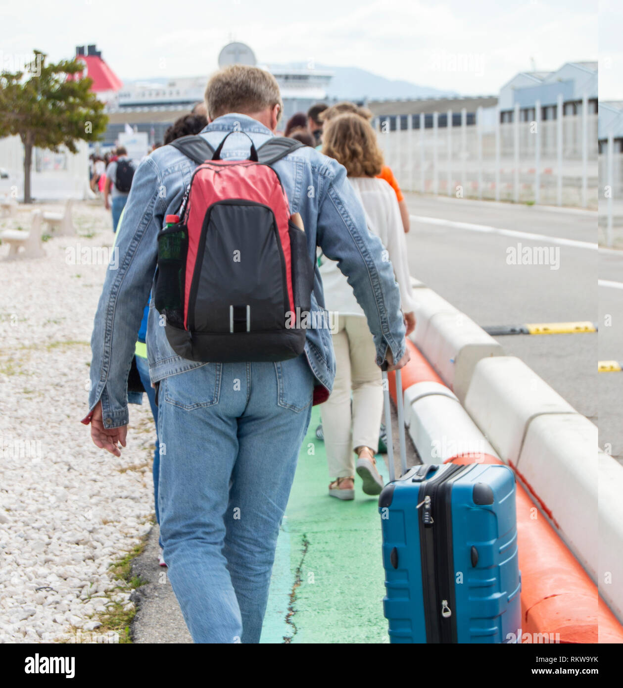 Happy tourists with backpacks and suitcases are moving along the road ...