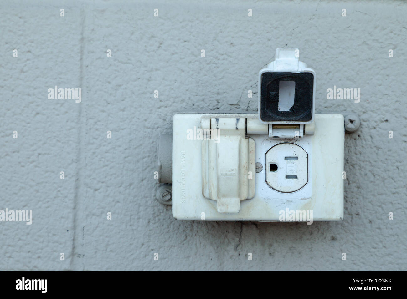 Old rustic North American electrical outlet on a exterior grey brick ...