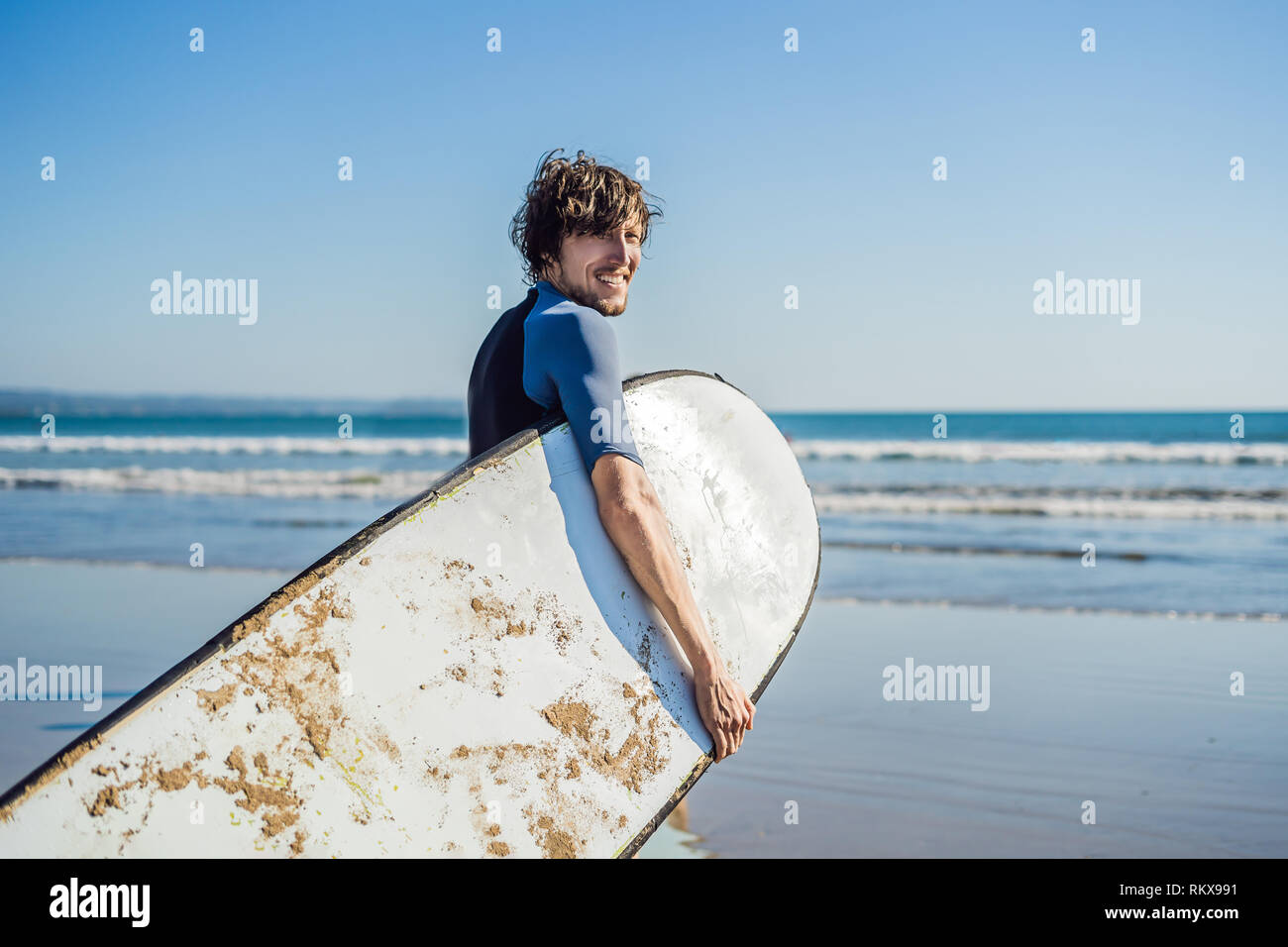 Handsome sporty young surfer posing with his surfboard under his arm in ...