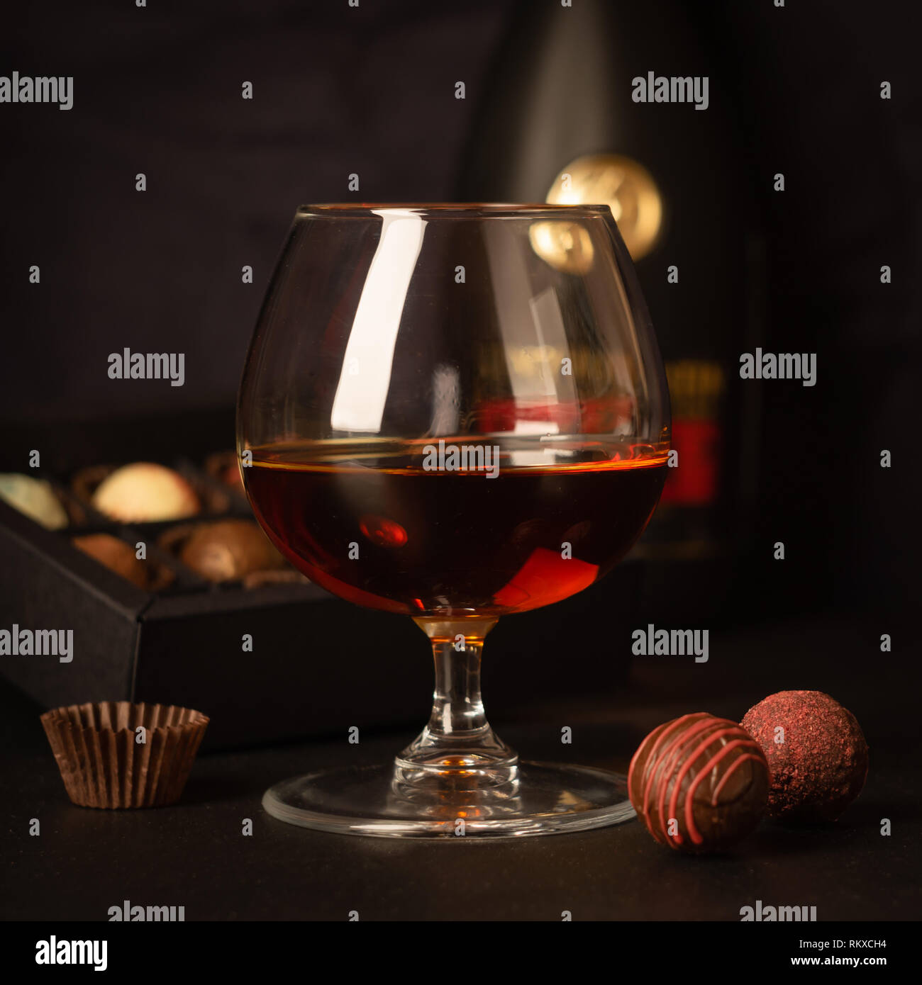 A glass of brandy and chocolate candy on dark background. Alcoholic ...