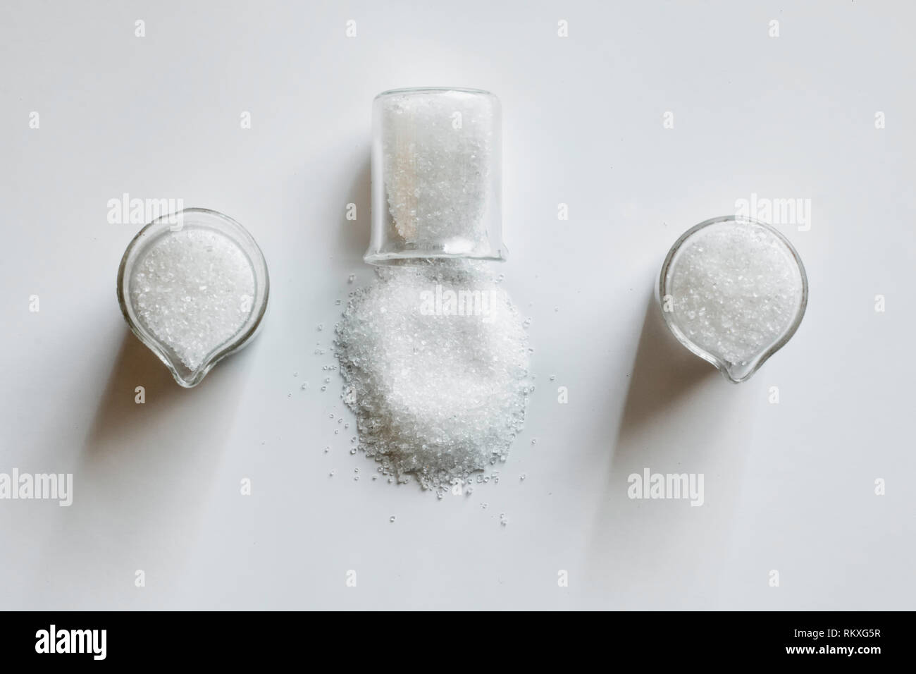 Three glass beakers of sugar on a white background, with one beaker ...