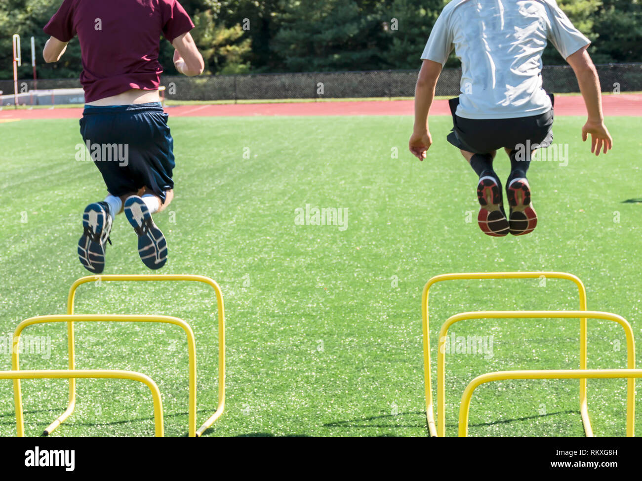 Two high school athletes bound over yellow hurdles on a green turf ...