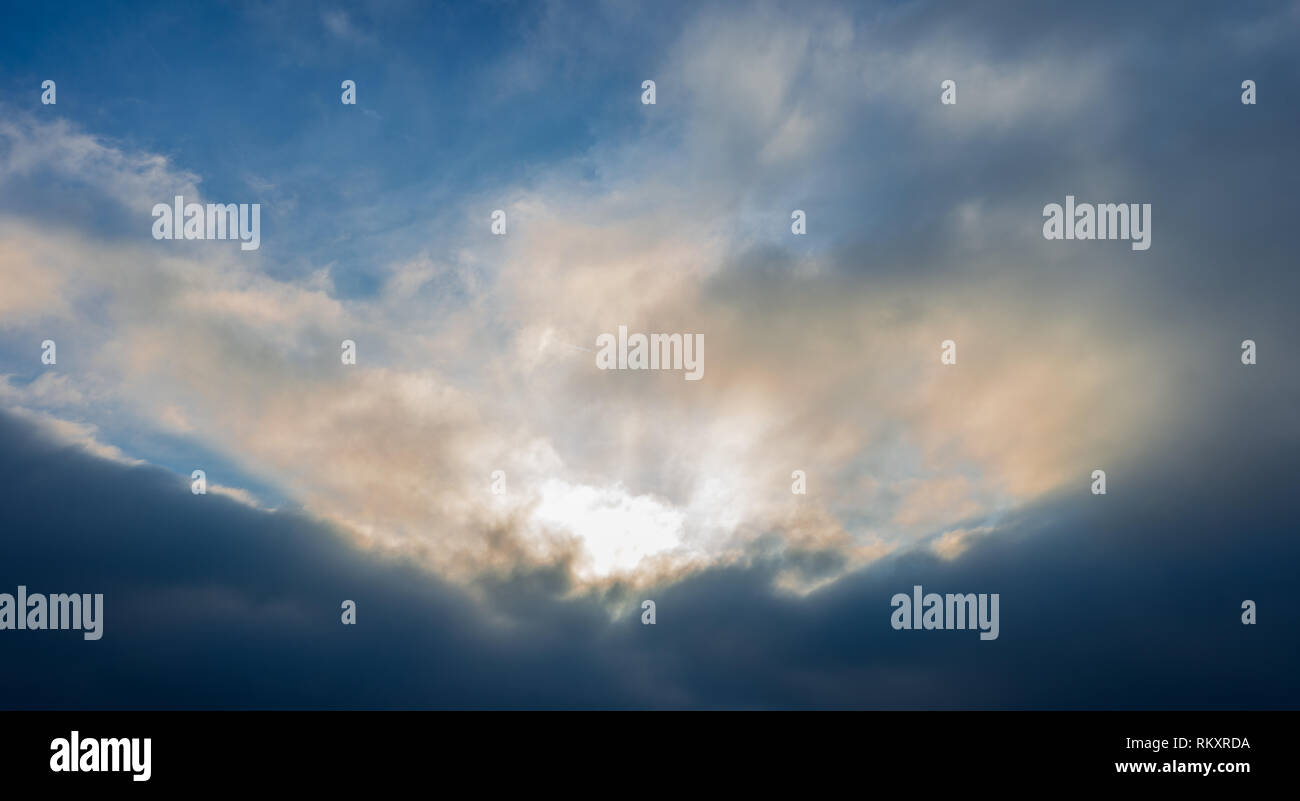 Dramatic cloudscape Sun piercing through the dark clouds and blue sky ...