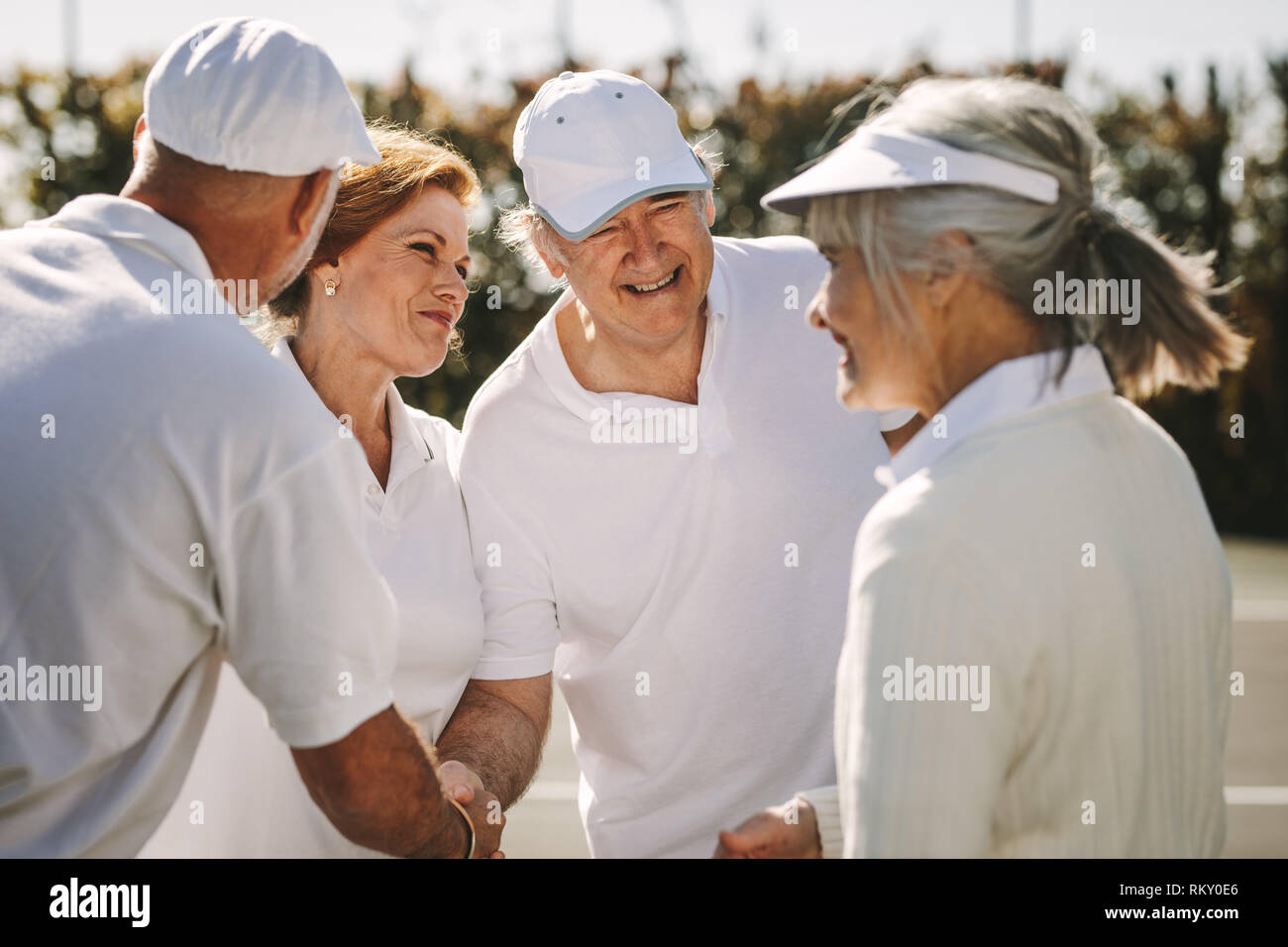 Smiling couples exchange greetings after a game of tennis. Senior ...