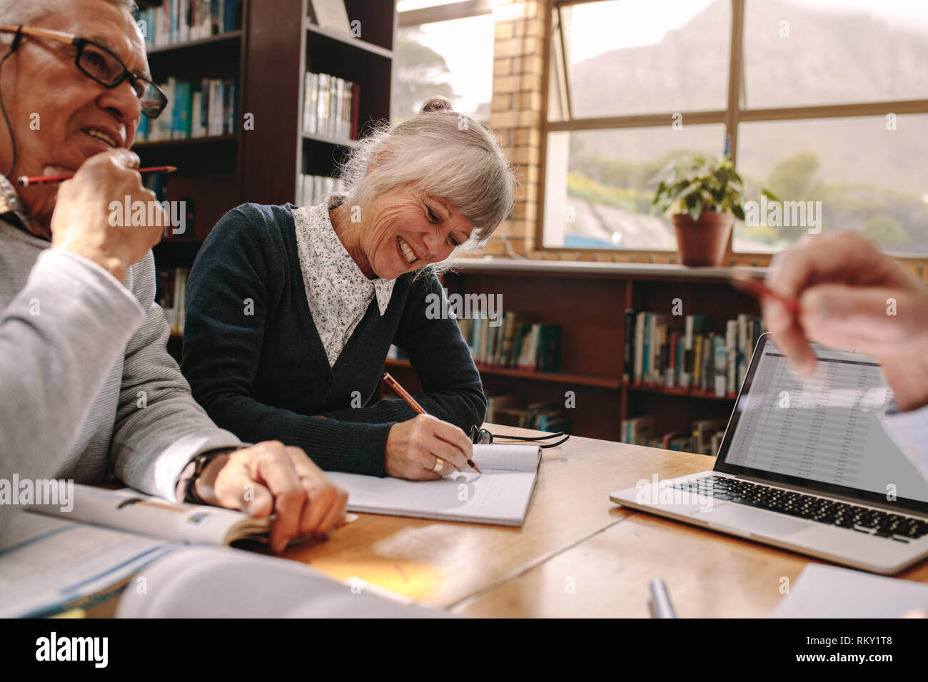 Senior woman writing notes sitting in a library with her male ...