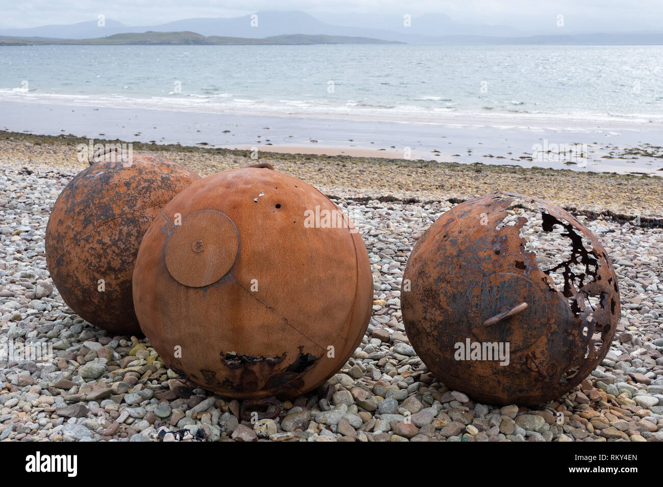 Three old and rusty buoys stranded on a pebble beach near the shoreline ...