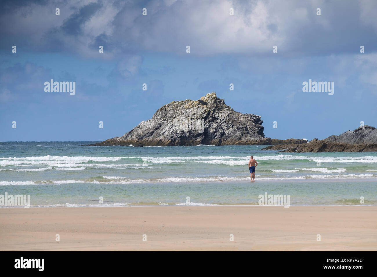A holidaymaker standing in the sea at Crantock Beach looking out to The ...